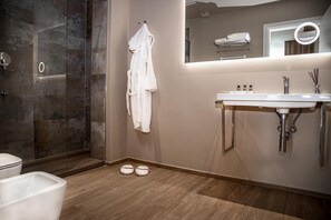Um banheiro moderno com box de vidro, banheira branca, espelho grande com iluminação circular e piso de madeira.