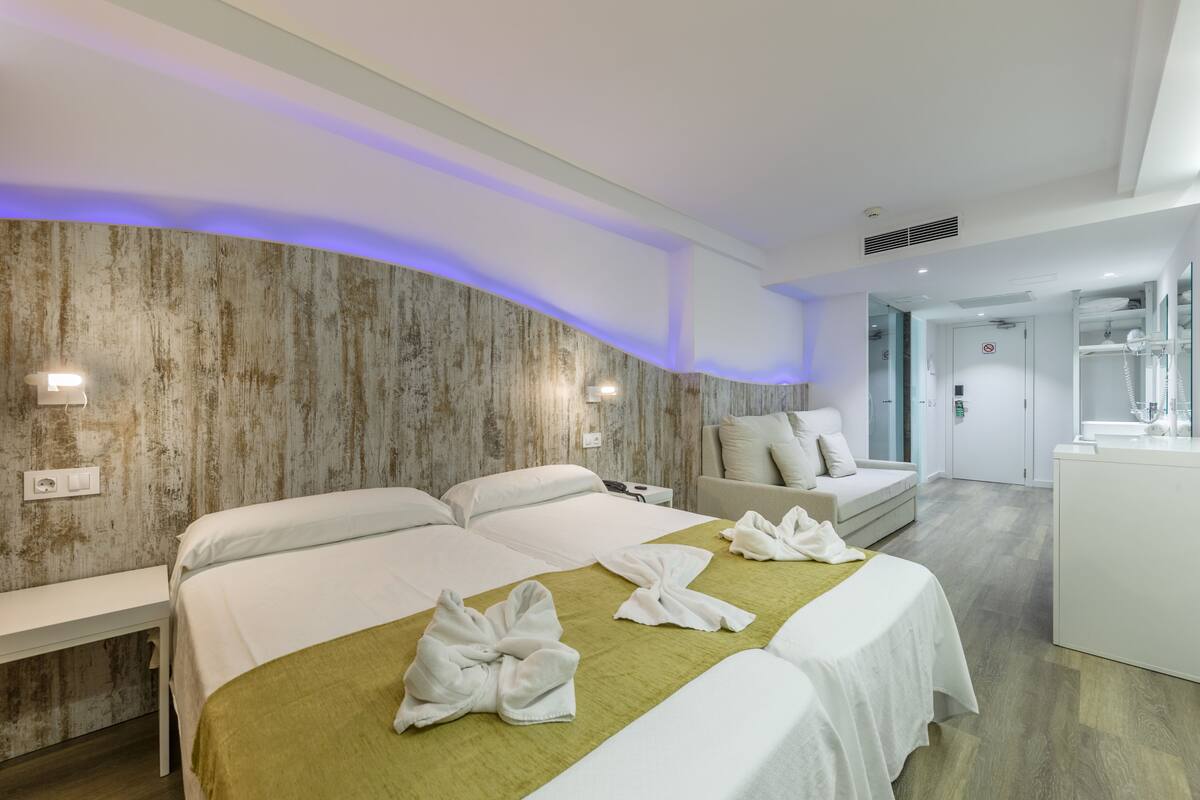 Quarto de hotel com uma cama grande, um sofá, uma escrivaninha e um banheiro visível através de uma porta aberta.