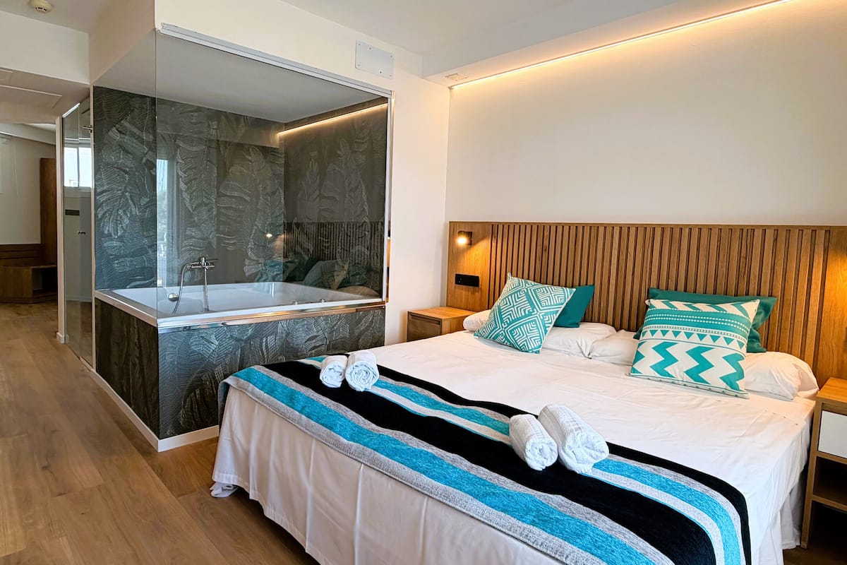 Quarto de hotel moderno com uma cama grande, área de chuveiro separada e cabeceira de madeira.