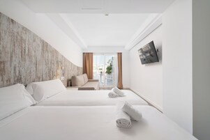 Quarto de hotel com duas camas, um sofá, uma televisão e vista para o exterior.