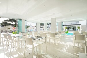 Uma área de refeições ao ar livre moderna, com cadeiras e mesas brancas, piscina ao fundo e vista da região.