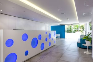 Uma área de recepção moderna com balcão branco e padrões circulares azuis, parede azul de destaque e vista para o exterior.