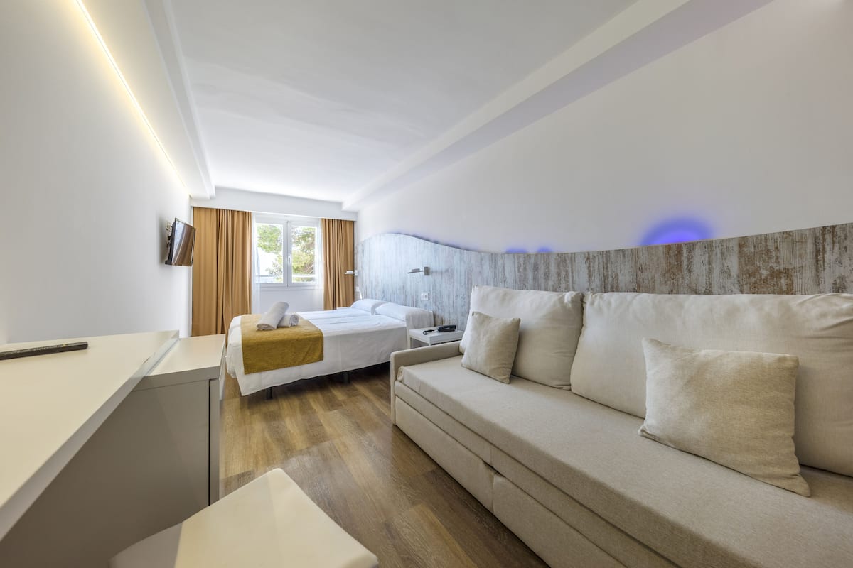 Quarto de hotel moderno com cama, sofá, escrivaninha e televisão.