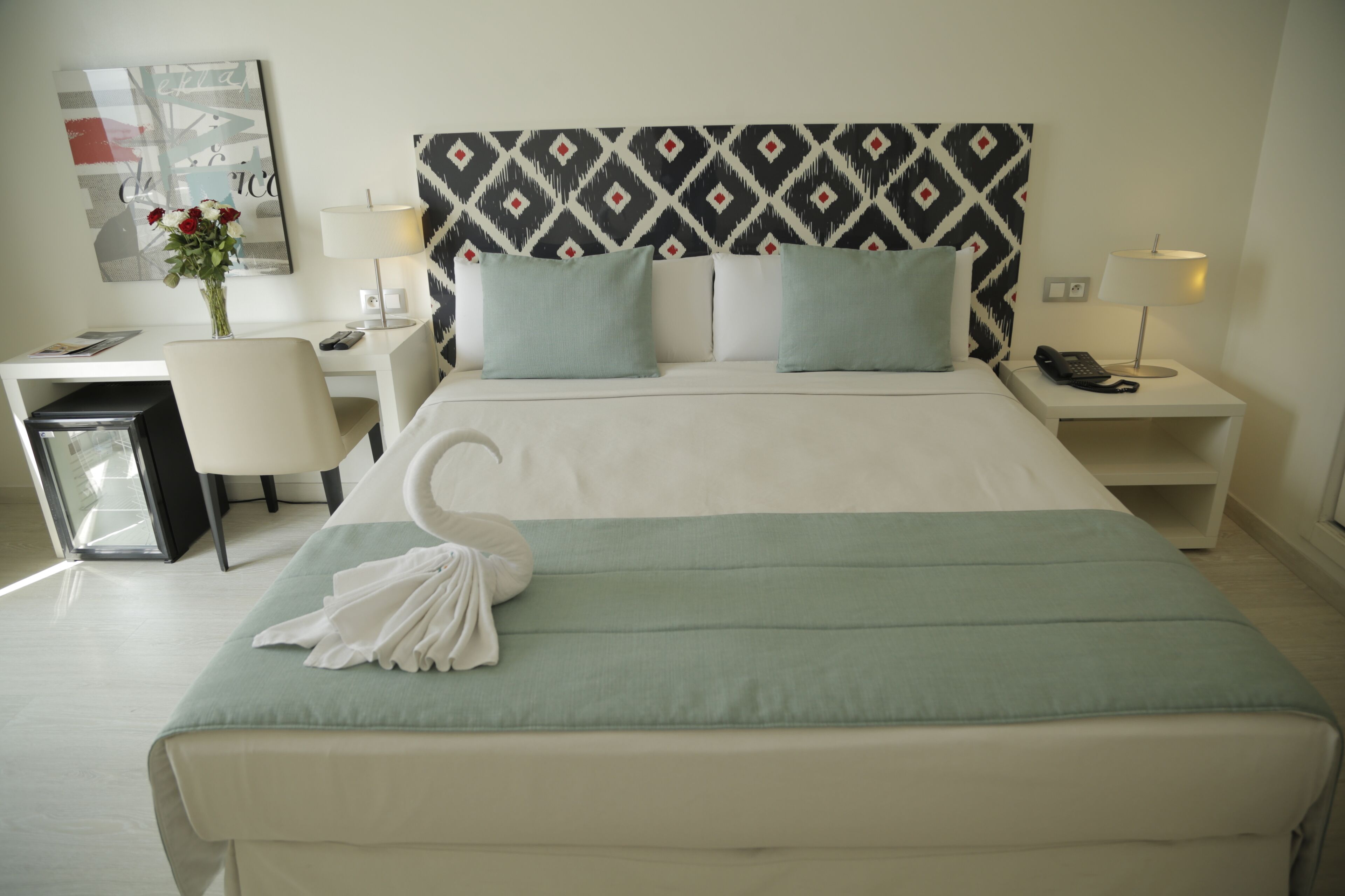 Quarto de hotel com uma cama grande, duas mesas de cabeceira, uma escrivaninha, uma cadeira e uma obra de arte pendurada na parede.