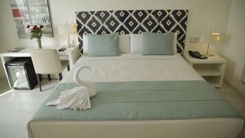 Quarto de hotel com uma cama grande, duas mesas de cabeceira, uma escrivaninha, uma cadeira e uma obra de arte pendurada na parede.