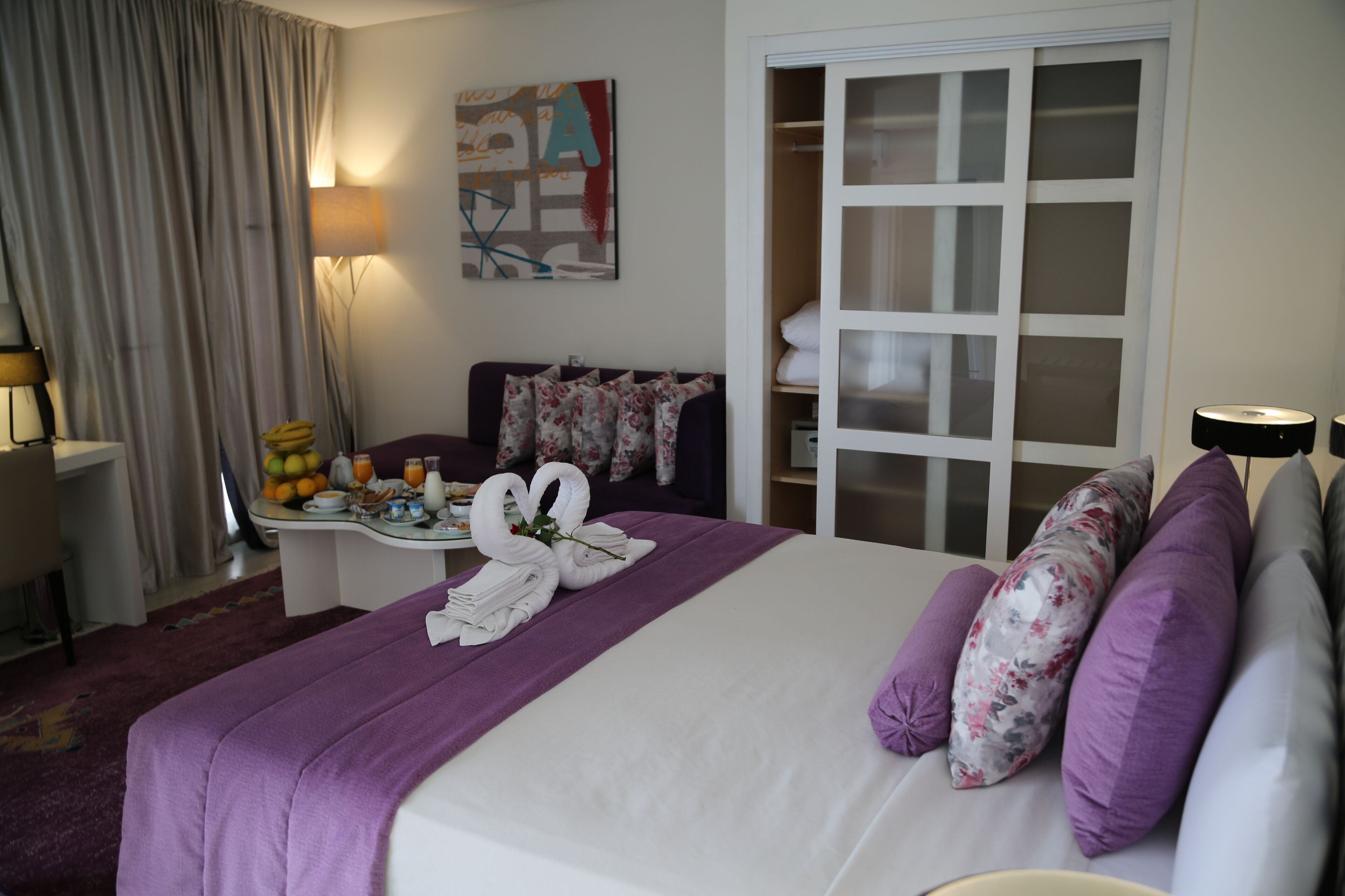 Quarto de hotel com cama bem arrumada, bandeja de café da manhã, escrivaninha e guarda-roupa.