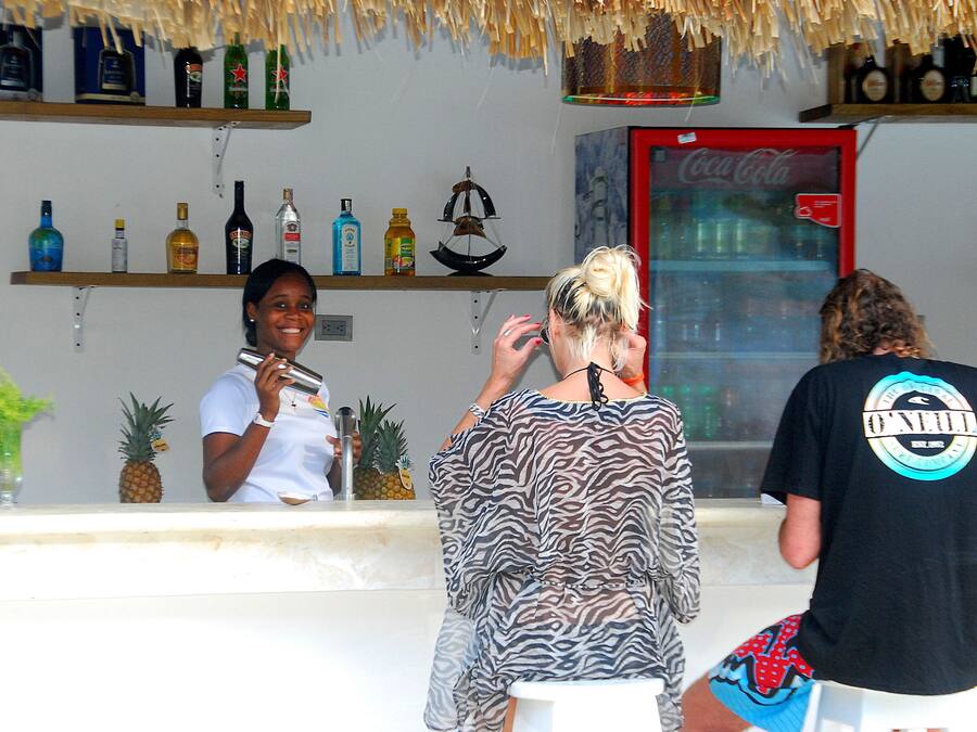 Uma área de bar com prateleiras de garrafas de bebidas, um refrigerador de Coca-Cola e uma decoração com abacaxi.