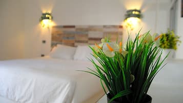 Quarto de hotel com cama bem arrumada, planta em vaso com flores brancas e duas luminárias na parede.