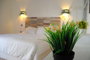 Quarto de hotel com cama bem arrumada, planta em vaso com flores brancas e duas luminárias na parede.