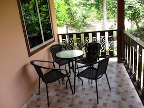 Uma área de estar coberta ao ar livre com mesa e cadeiras, vista para o verde lá fora e piso de azulejos.