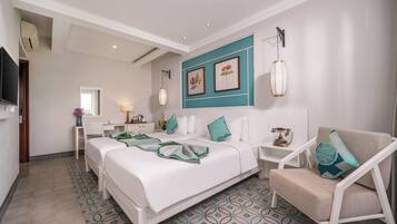 Quarto de hotel com cama, escrivaninha, cadeira, televisão e luminária fixada na parede.