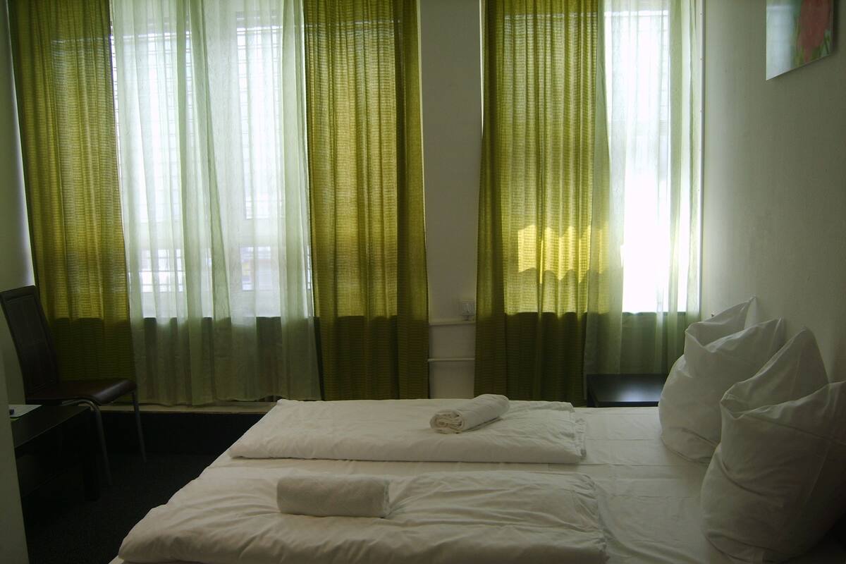 Quarto de hotel com cama, uma cadeira e cortinas.