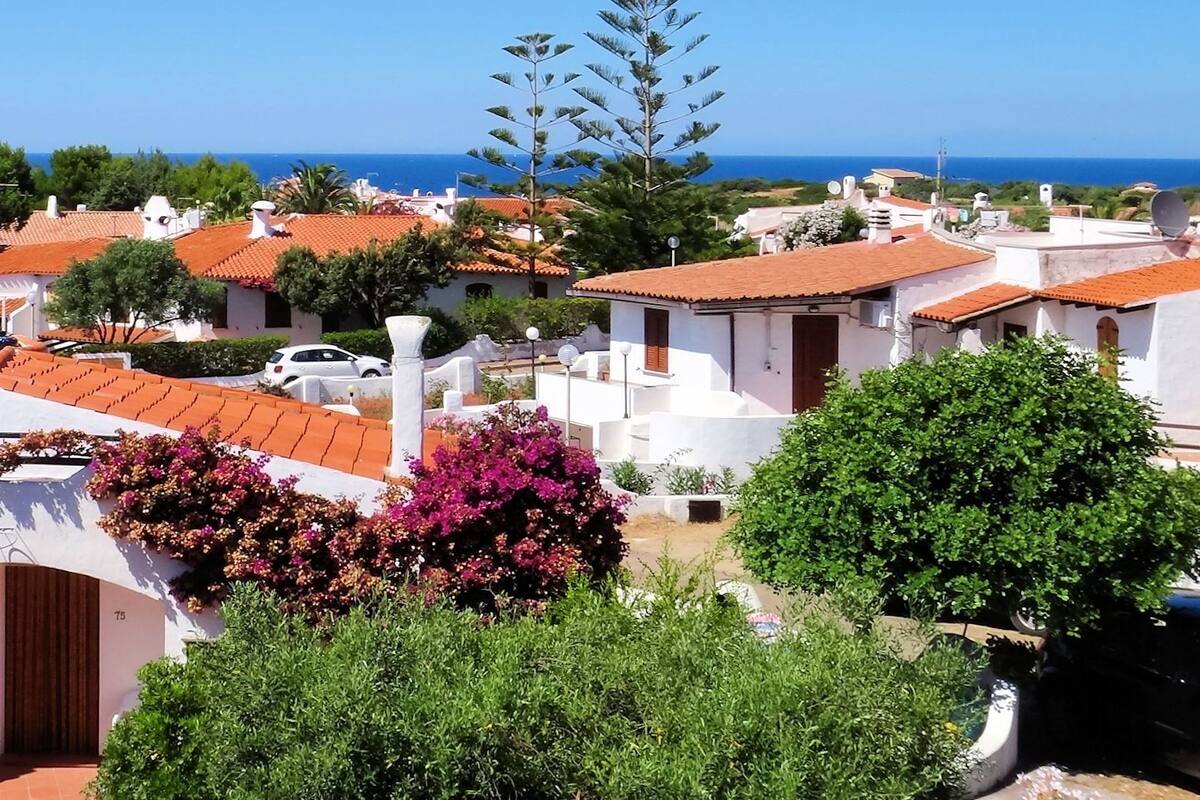 Uma área residencial costeira com edifícios brancos, telhados de telha vermelha e vista clara do mar.