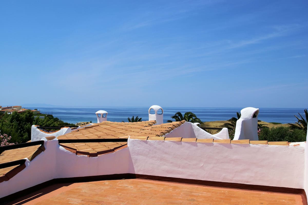 Terraço no telhado com telhas de barro, paredes brancas e vista para o mar.