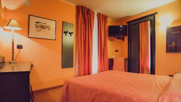 Quarto de hotel com cama, escrivaninha, luminária, televisão e quadro na parede.
