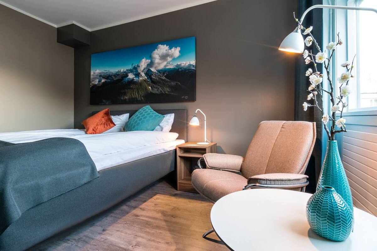 Quarto de hotel moderno com uma cama, uma cadeira, uma mesa e um vaso.