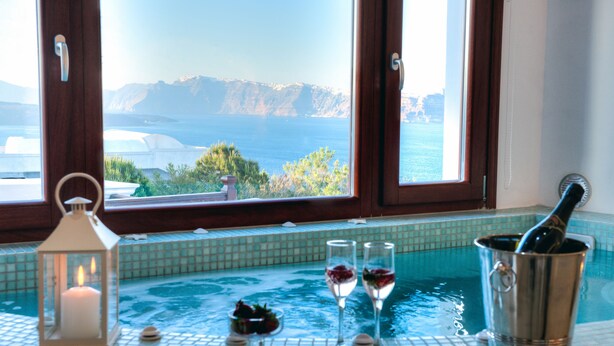 Uma área de piscina com vista para o mar, uma vela, dois copos de vinho e uma garrafa de champanhe.
