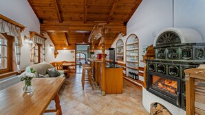 Uma cozinha acolhedora com um fogão a lenha, uma área de jantar com uma mesa comprida e um bar com prateleiras cheias de garrafas.