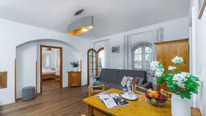 Sala moderna com mesa de jantar de madeira, sofá cinza e uma janela grande com cortinas leves.