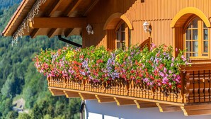 Uma chalé de madeira com varanda decorada com flores coloridas, fachada de madeira e montanhas ao fundo.