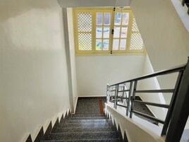 Uma escada com corrimão, uma janela com treliça e um ventilador de teto.