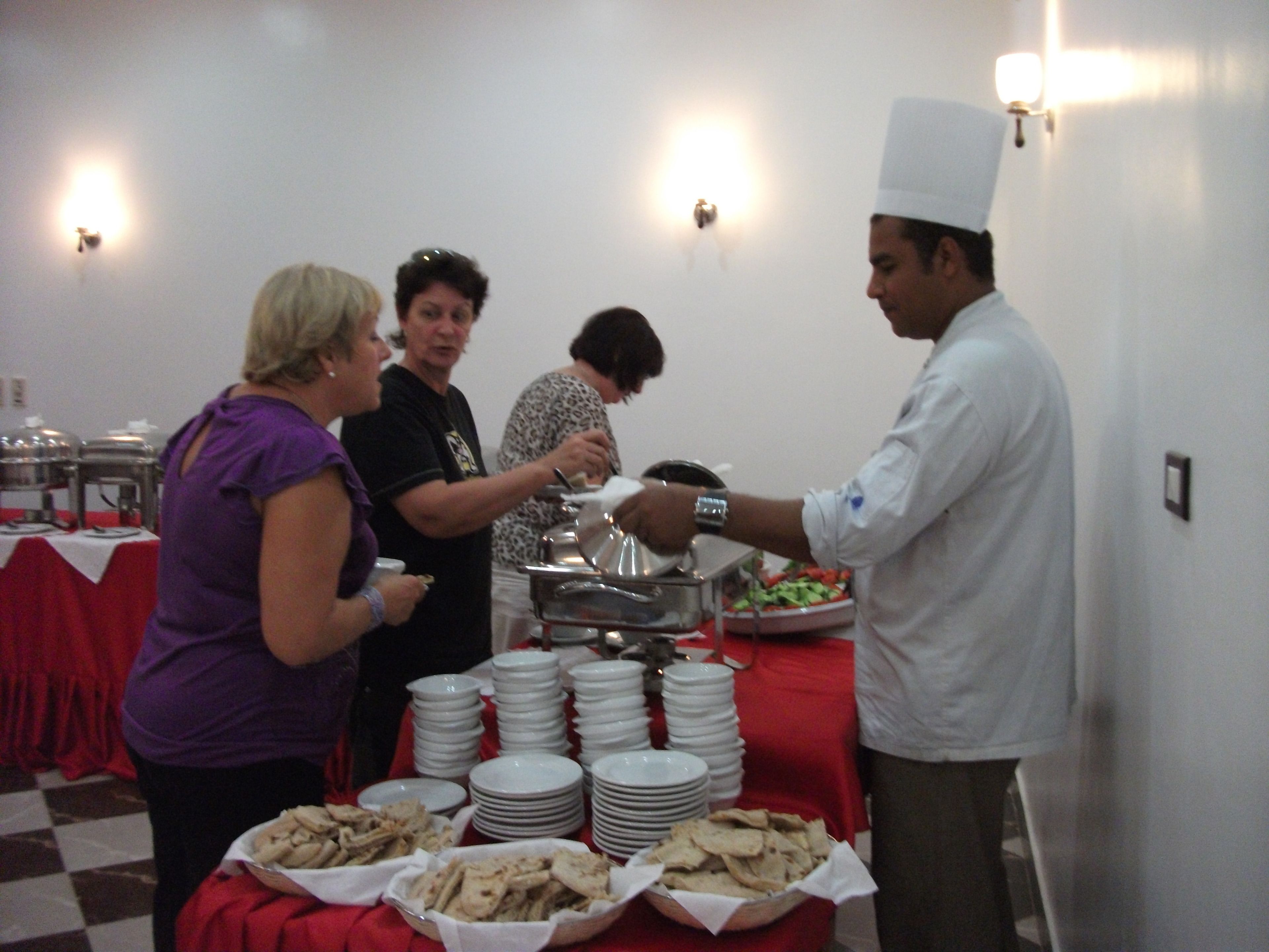 Uma mesa de buffet com vários pontos de comida e pessoas presentes.