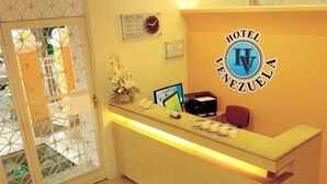 Bancada de recepção de hotel com um relógio, um computador e um telefone.