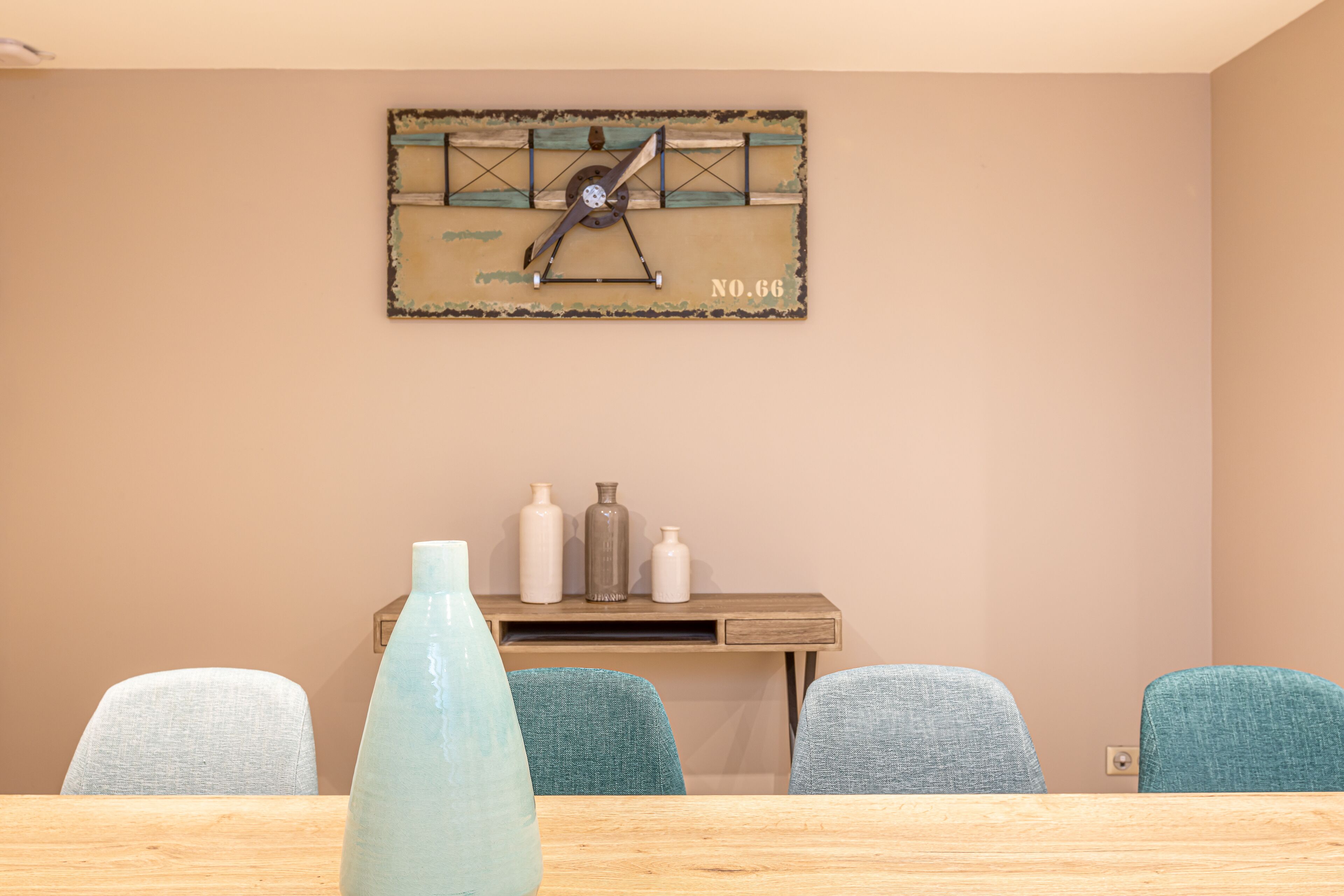 Uma sala de jantar com uma mesa de madeira, cadeiras cor turquesa e um relógio antigo na parede.