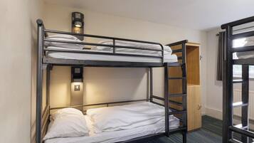 Uma cama beliche com escada, luminária sobre o colchão superior e um armário de madeira no canto.