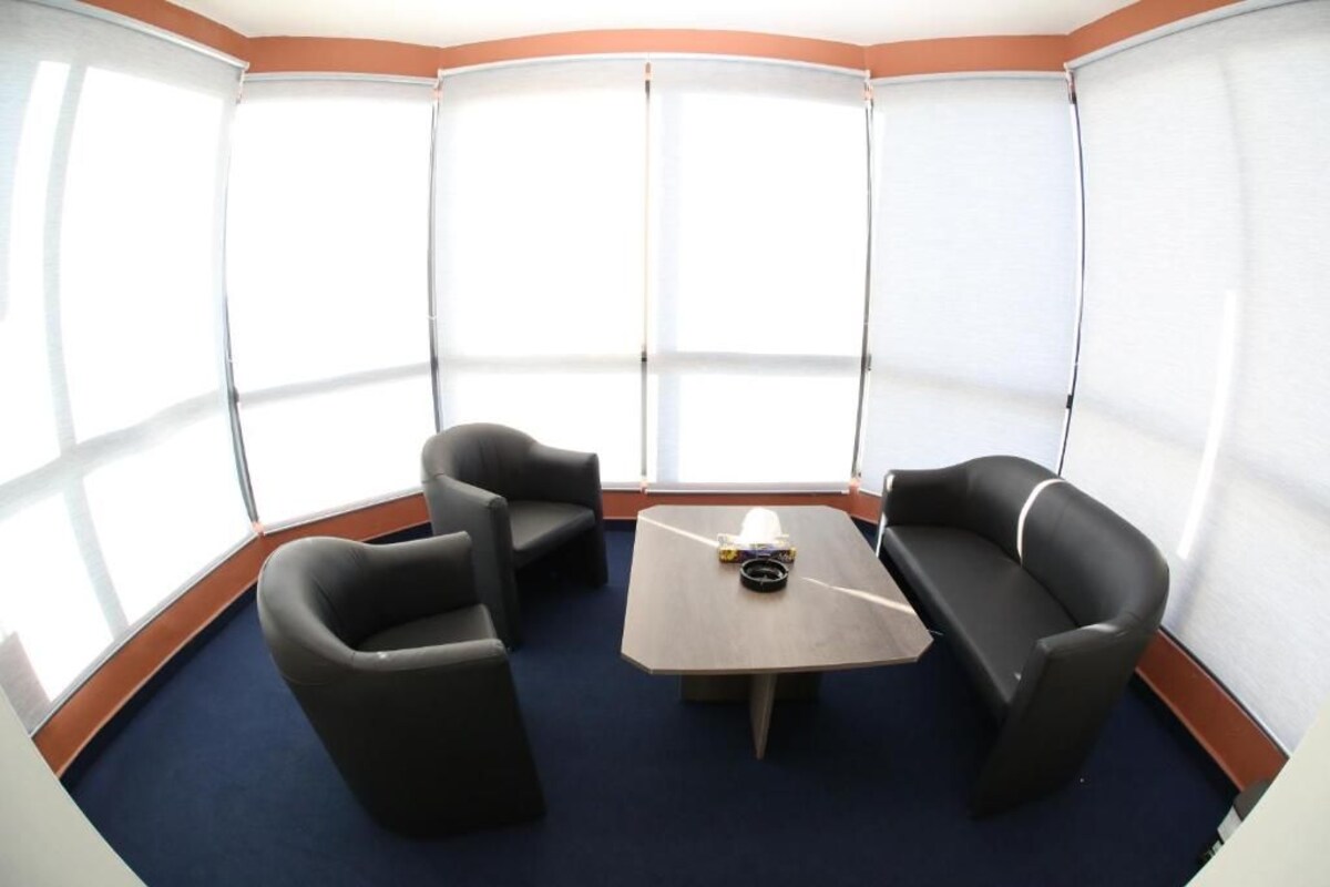 Quarto de canto com dois sofás e uma pequena mesa, janelas amplas e um tapete azul.