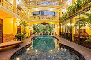 Piscina interior com cobertura de vidro, rodeada por paredes amarelas e grades de madeira.