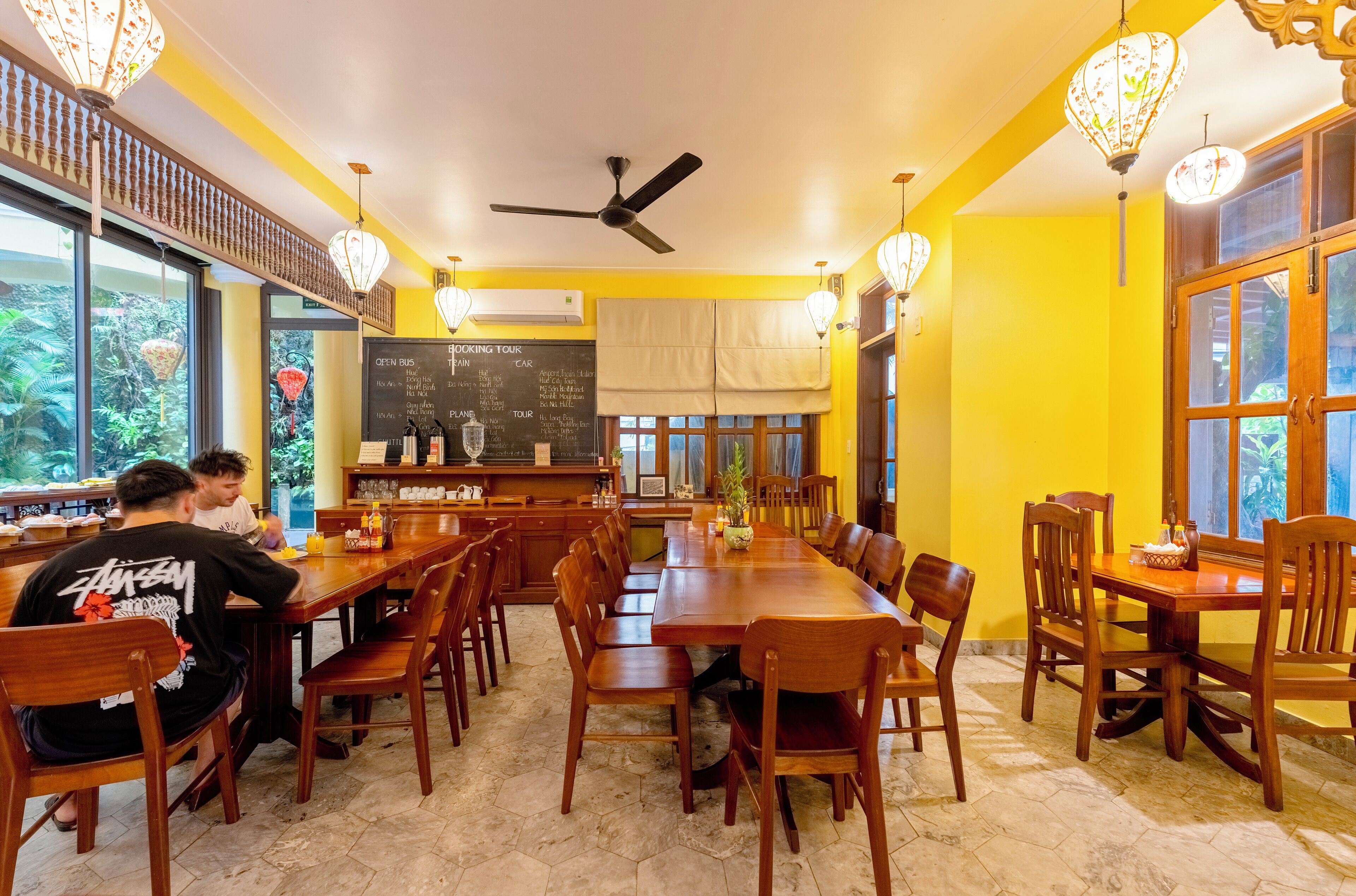 Um restaurante com uma mesa de madeira comprida, várias cadeiras e lanternas de papel penduradas.