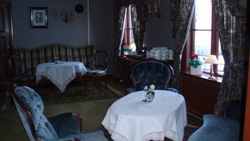 Um quarto com uma mesa de jantar posta para dois, um sofá e uma cadeira com um vaso de flores.