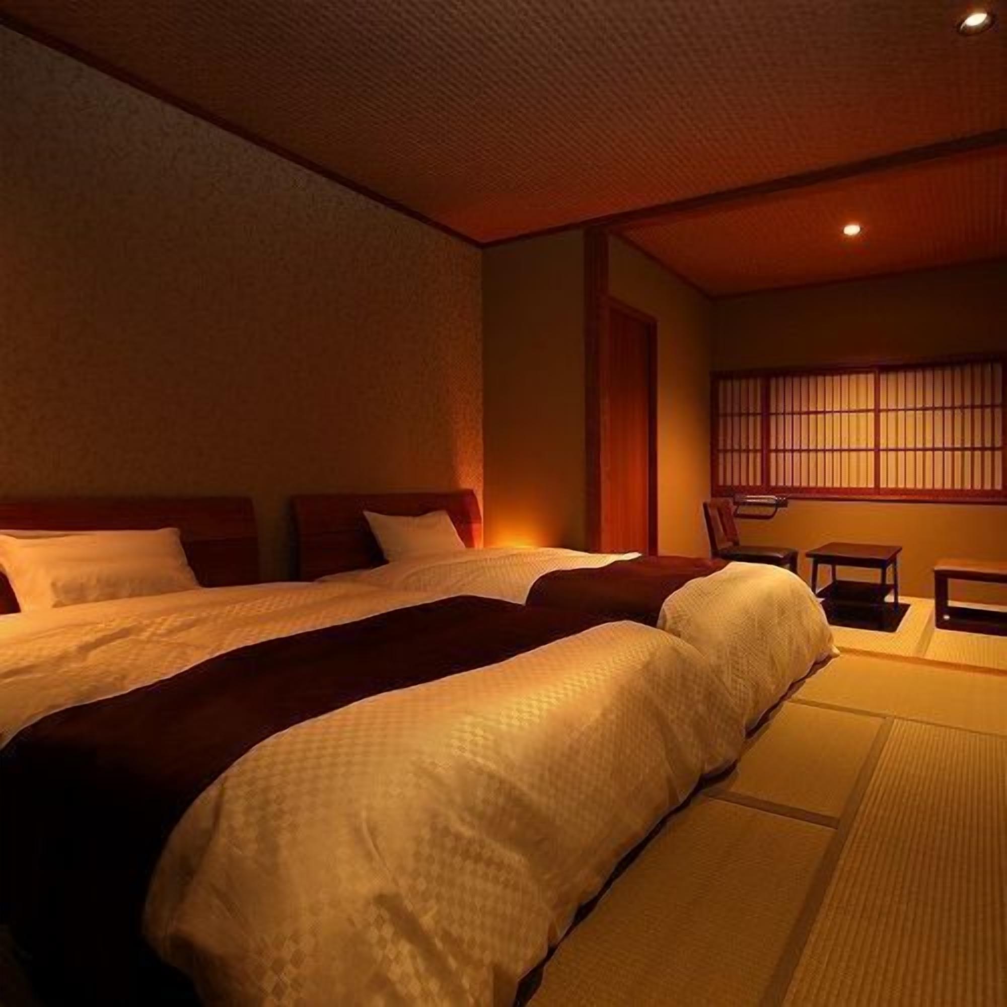 Quarto de hotel com duas camas, uma janela com persianas tradicionais e uma pequena mesa.