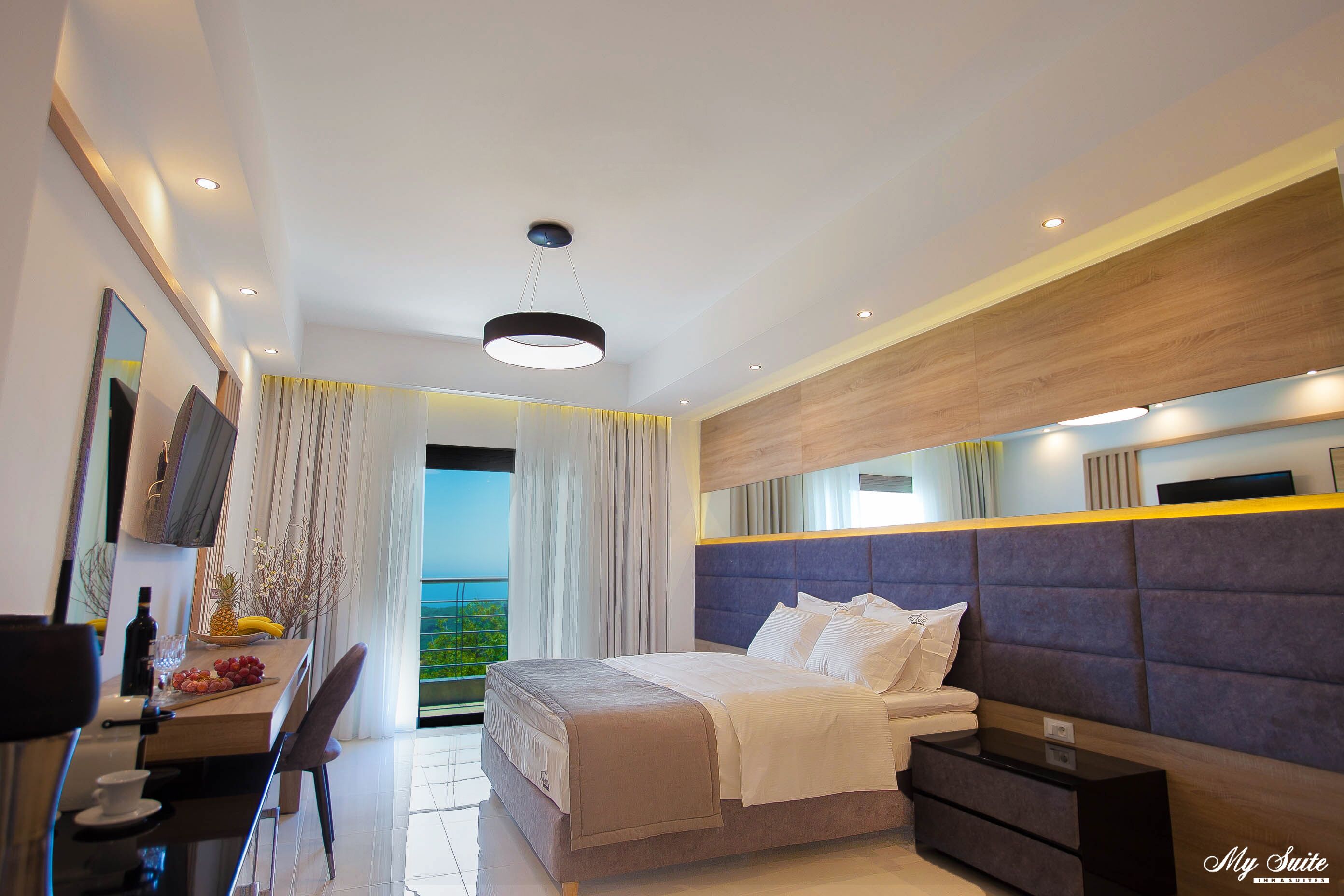 Quarto moderno com cama, mesas de cabeceira, escrivaninha e uma janela grande com cortinas.