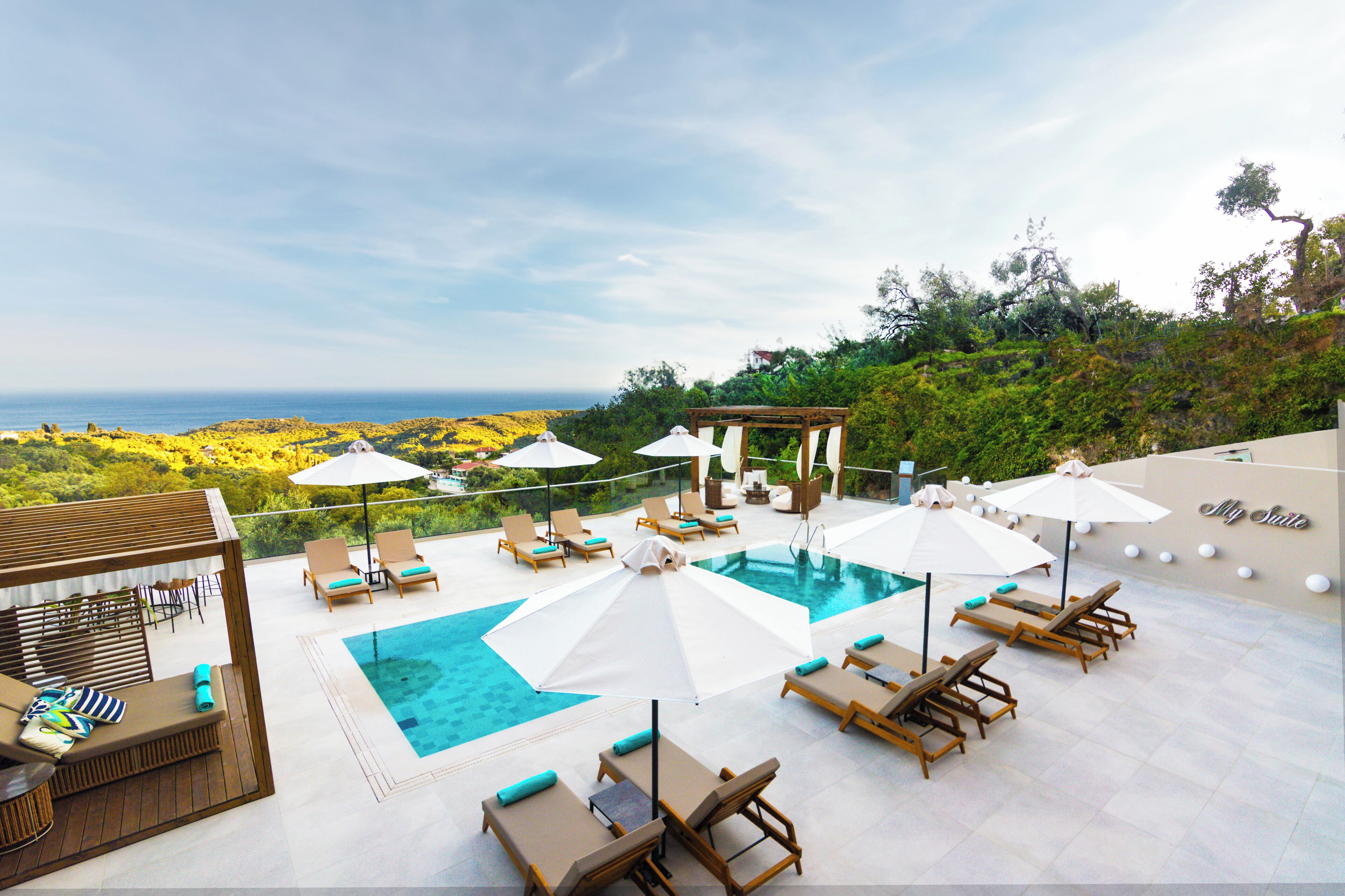 Uma área de piscina no terraço com espreguiçadeiras, guarda-sóis e vista para o mar.