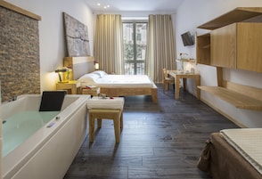 Quarto de hotel com uma cama grande, uma escrivaninha de madeira, televisão, banheira e varanda com cortinas.