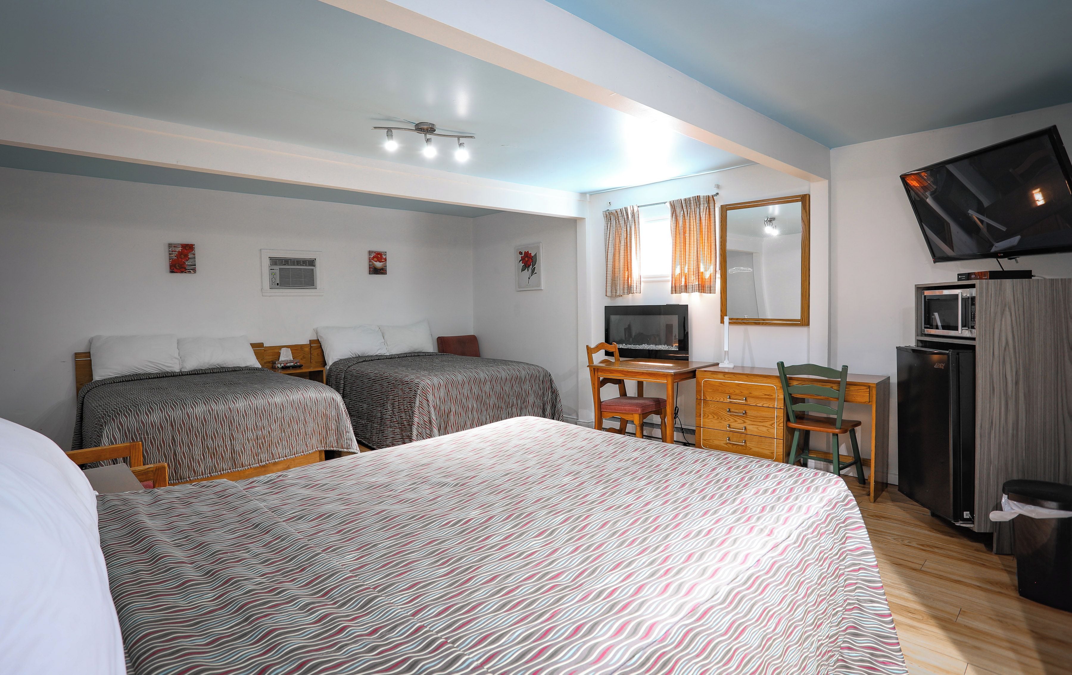 Quarto de hotel com duas camas, uma escrivaninha com cadeira, televisão, espelho e micro-ondas.