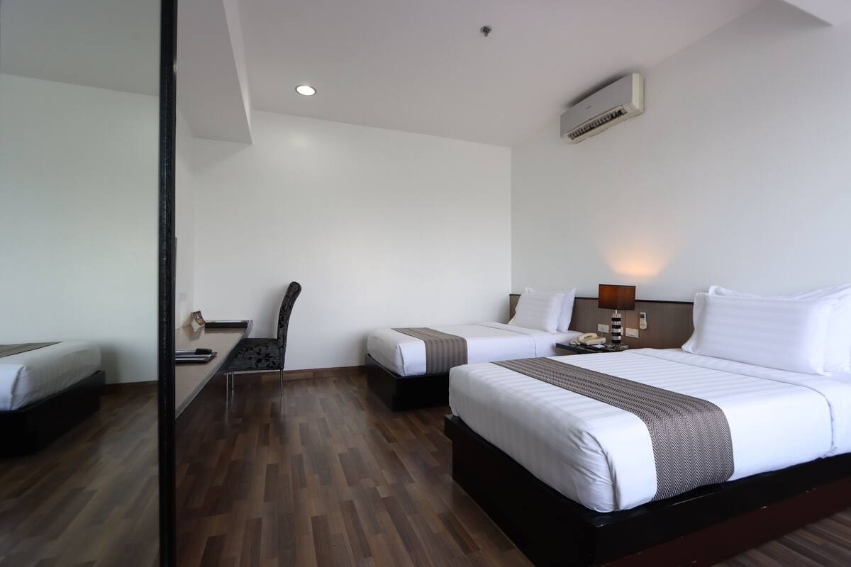 Quarto de hotel com duas camas, uma escrivaninha, uma cadeira e um ar condicionado na parede.