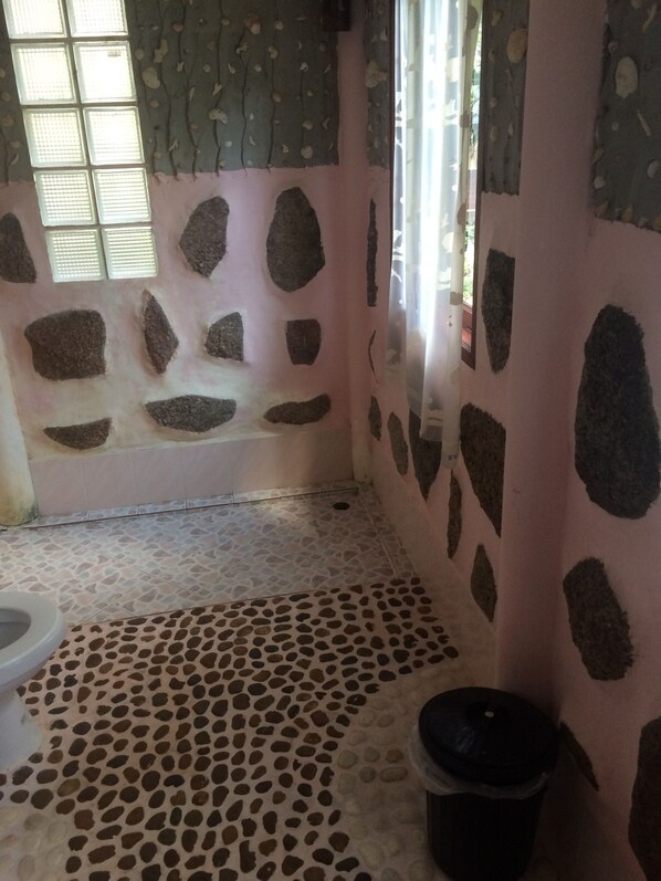 Casa de banho com design único na parede de pedra, soalho estampado e sanita.