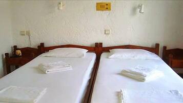 Quarto duplo com duas camas, cada uma com colchão e almofadas brancas, cabeceiras de madeira e mesas de cabeceira.
