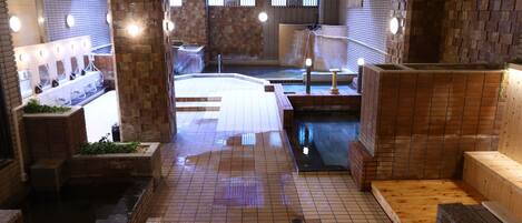 Um onsen japonês tradicional com várias piscinas termais, bancos de madeira e pavimento ladrilhado.