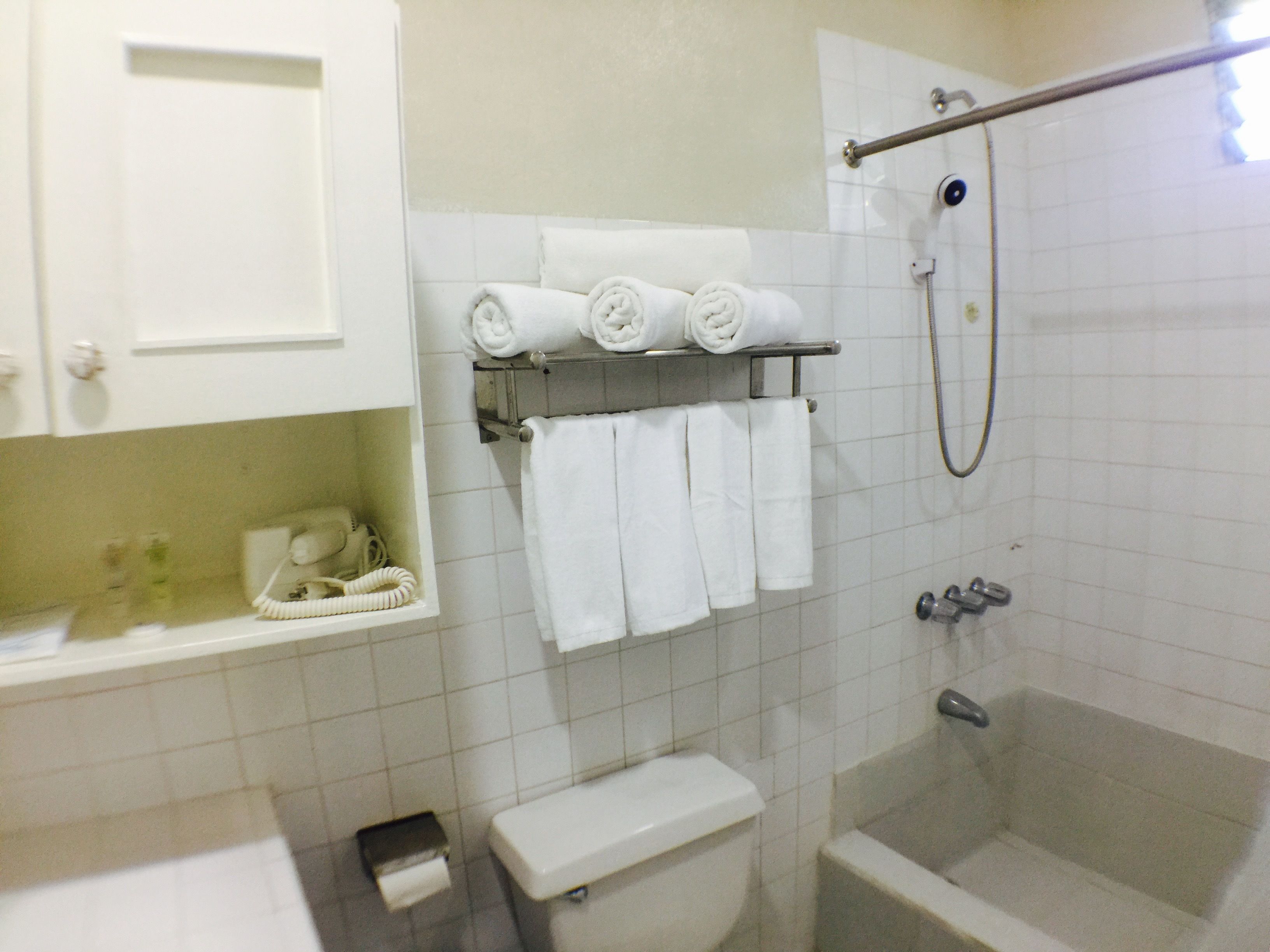 Casa de banho com sanita, lavatório e chuveiro. Há toalhas num suporte e um rolo de papel higiénico.