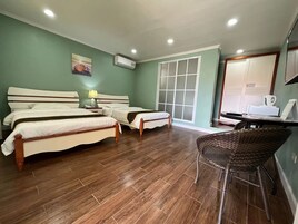 Quarto de hotel com duas camas, uma cadeira de vime, uma escrivaninha com computador e uma janela grande.