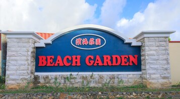 Placa para um jardim à beira-mar, com um muro de pedra e um céu azul claro ao fundo.