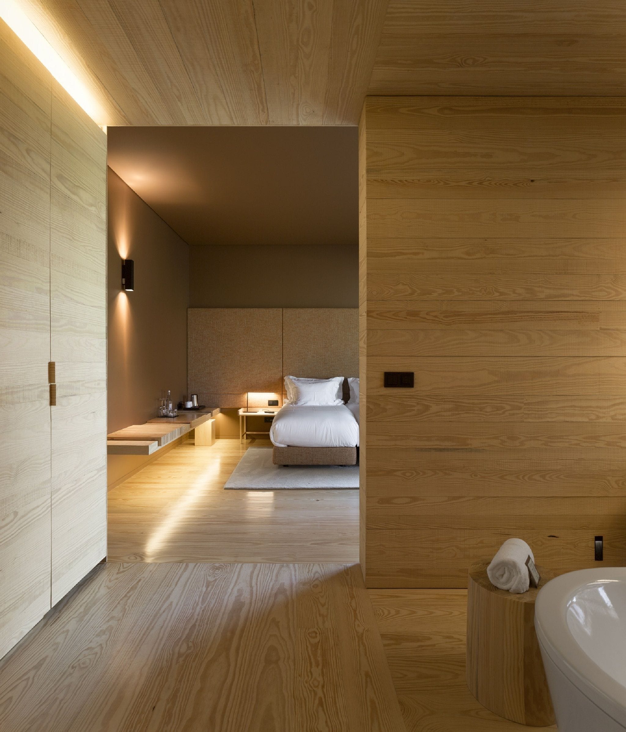 Quarto moderno com piso de madeira, uma cama, uma mesa de cabeceira e um criado-mudo.