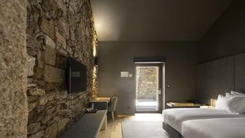Um quarto moderno com parede de pedra, um banco de madeira, uma cama e uma TV.