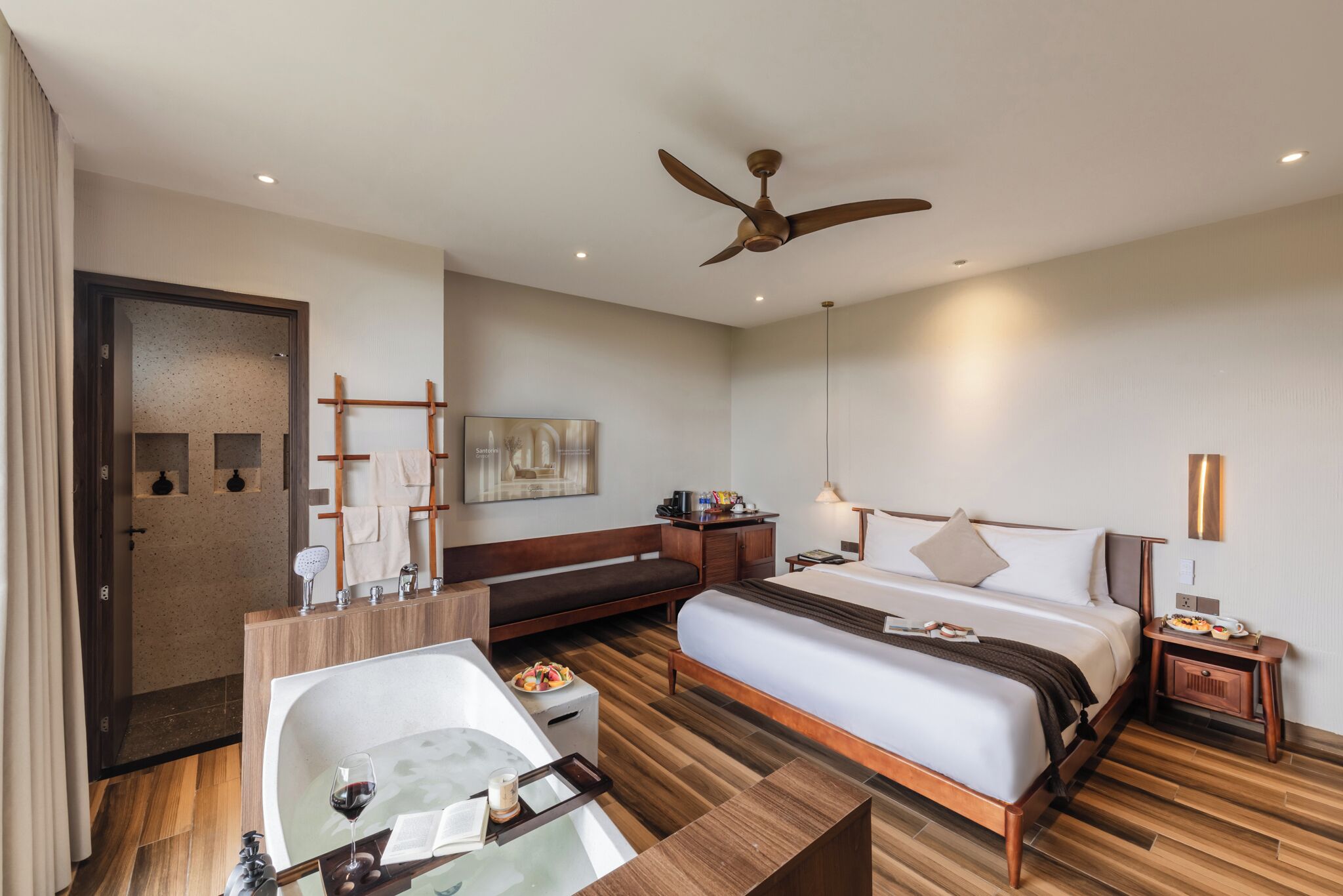 Quarto de hotel com cama grande, área de estar, banheira e ventoinha no teto.