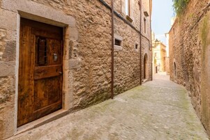 Uma rua de paralelepípedos estreita, ladeada por edifícios de pedra com portas de madeira e janelas pequenas.