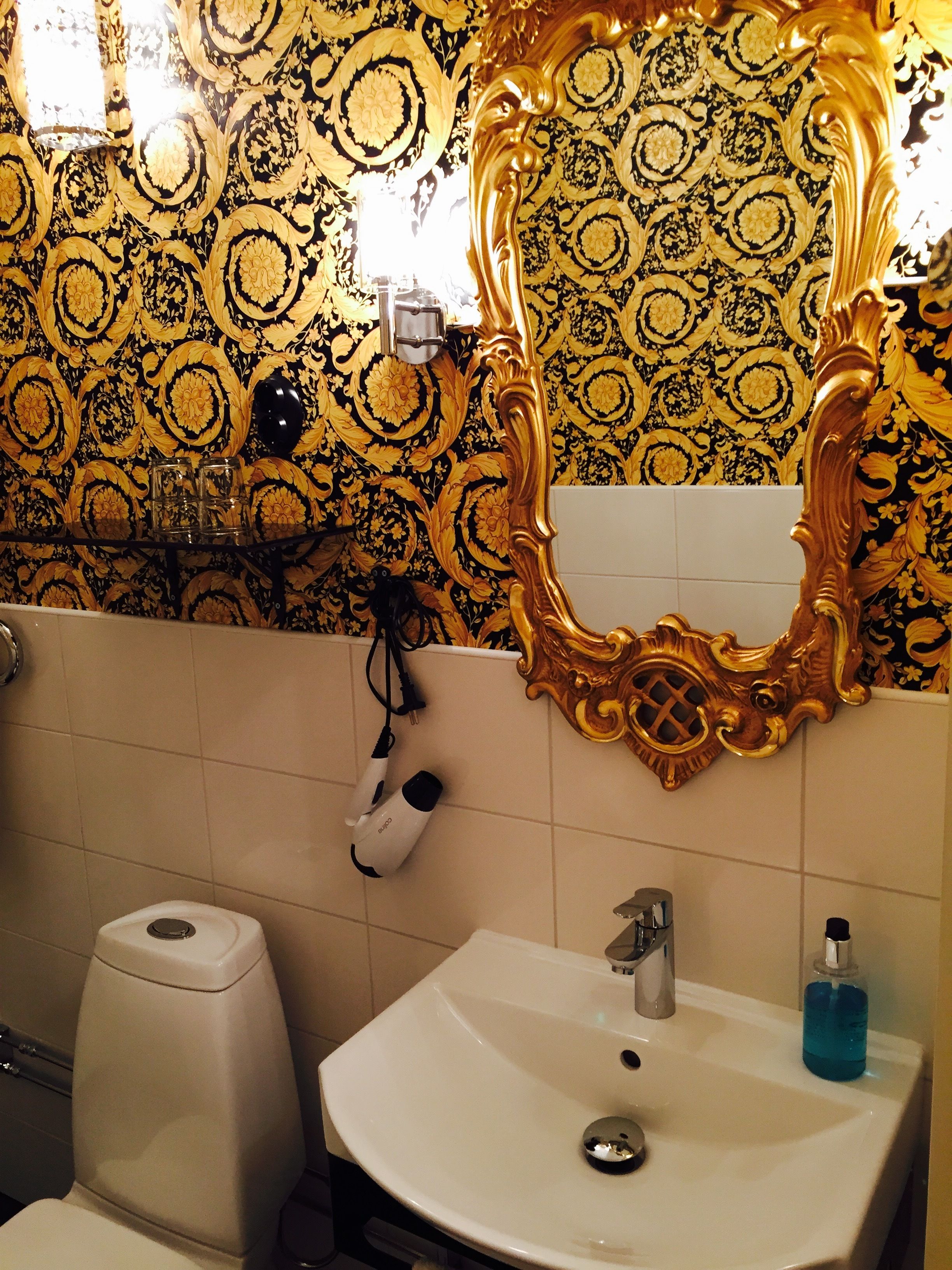 Uma casa de banho com uma pia branca, um espelho com moldura ornamentada e uma sanita.